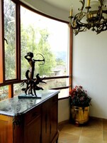 Quarto com armário de madeira, bancada de mármore, escultura em bronze, planta em vaso com flores vermelhas e um candelabro.