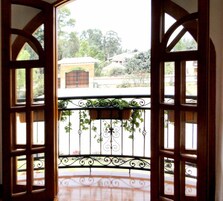 Uma porta de madeira aberta com vista para uma varanda com grade de metal e plantas penduradas.