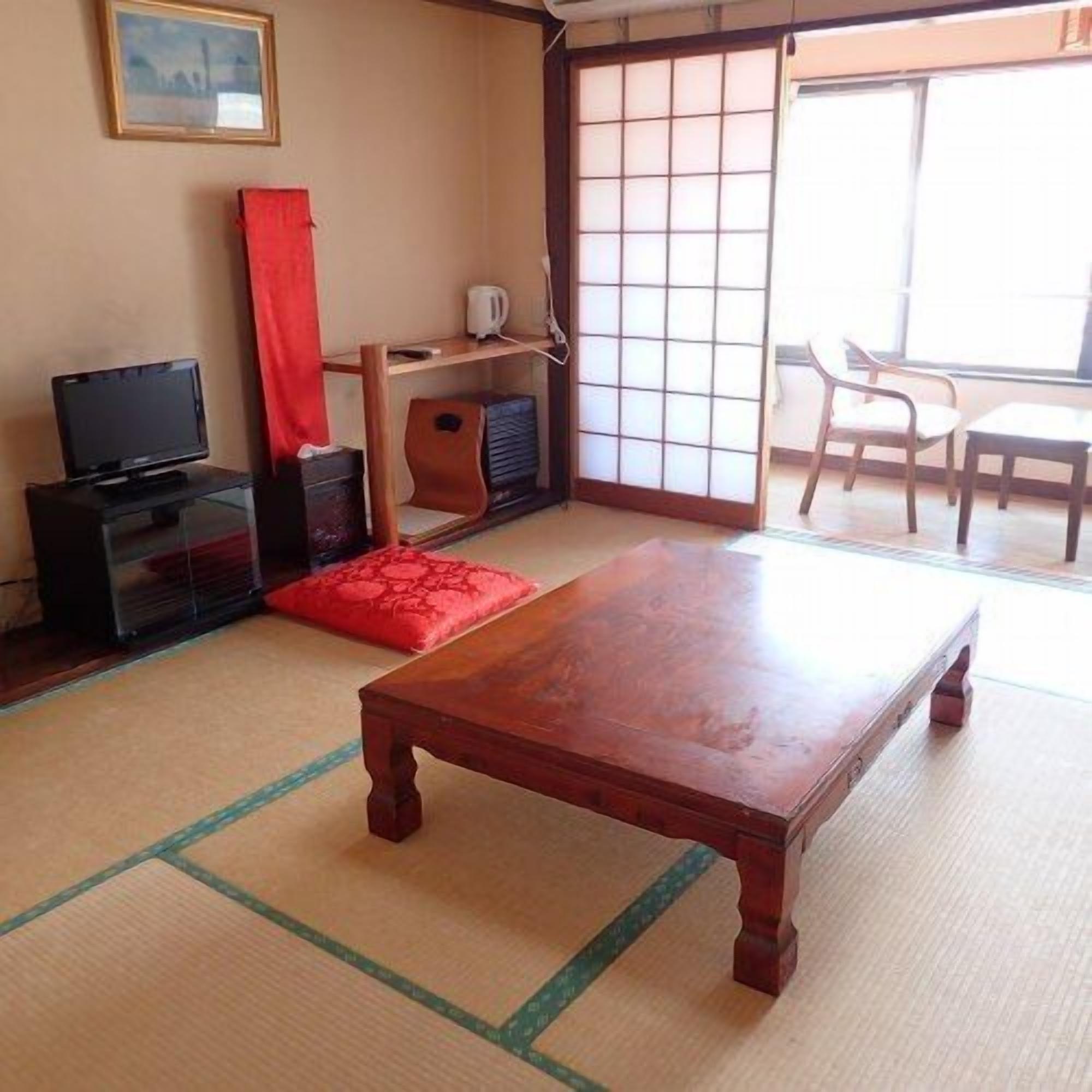 Quarto japonês tradicional com tatames, uma mesa de madeira, uma televisão e uma porta deslizante.