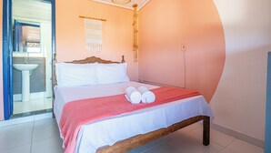 Quarto com cama, mesa de cabeceira, luminária pendente e vista para um banheiro.