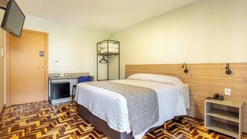 Quarto de hotel com cama, escrivaninha, cadeira, guarda-roupa e televisão.