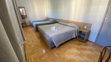 Quarto de hotel com duas camas, um chão de madeira em padrão herringbone, uma mesa de cabeceira e um espelho.
