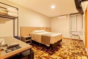 Quarto de hotel com cama, mesa de cabeceira e escrivaninha com cadeira.