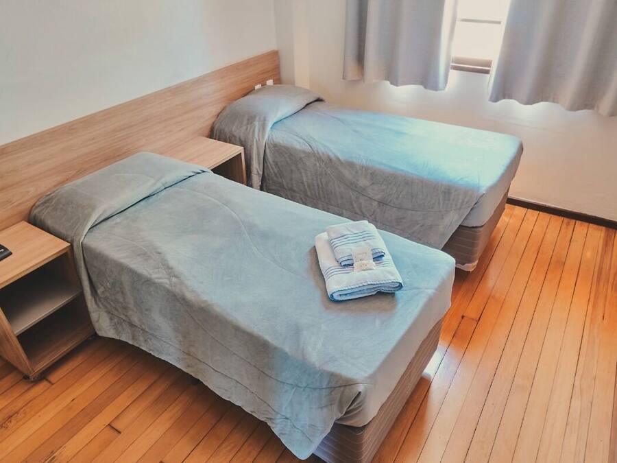 Quarto com duas camas, uma mesa de cabeceira com telefone e uma janela com cortinas.