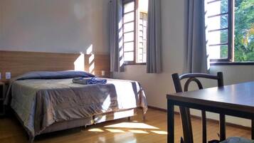 Quarto com cama, mesa e janela com cortinas.