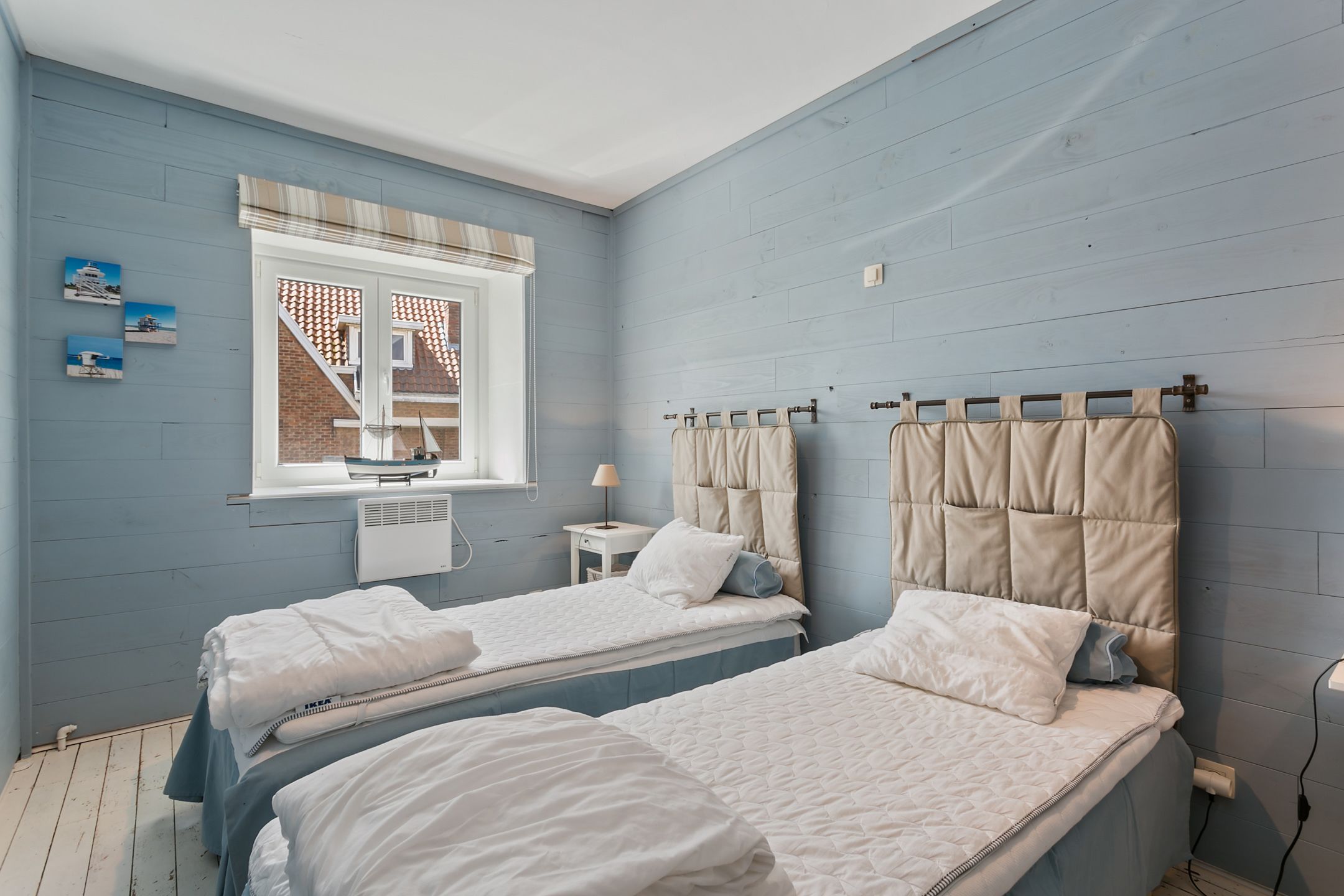 Quarto com duas camas, uma janela com vista para um edifício de tijolos e uma pequena mesa com abajur.