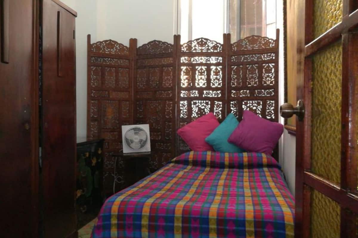 Quarto com uma cama, um painel de madeira e um ventilador.