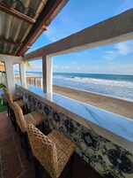 Um bar à beira-mar com cadeiras de vime e vista para o oceano.
