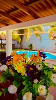 Área na piscina com teto de madeira e vista para a piscina e palmeiras.