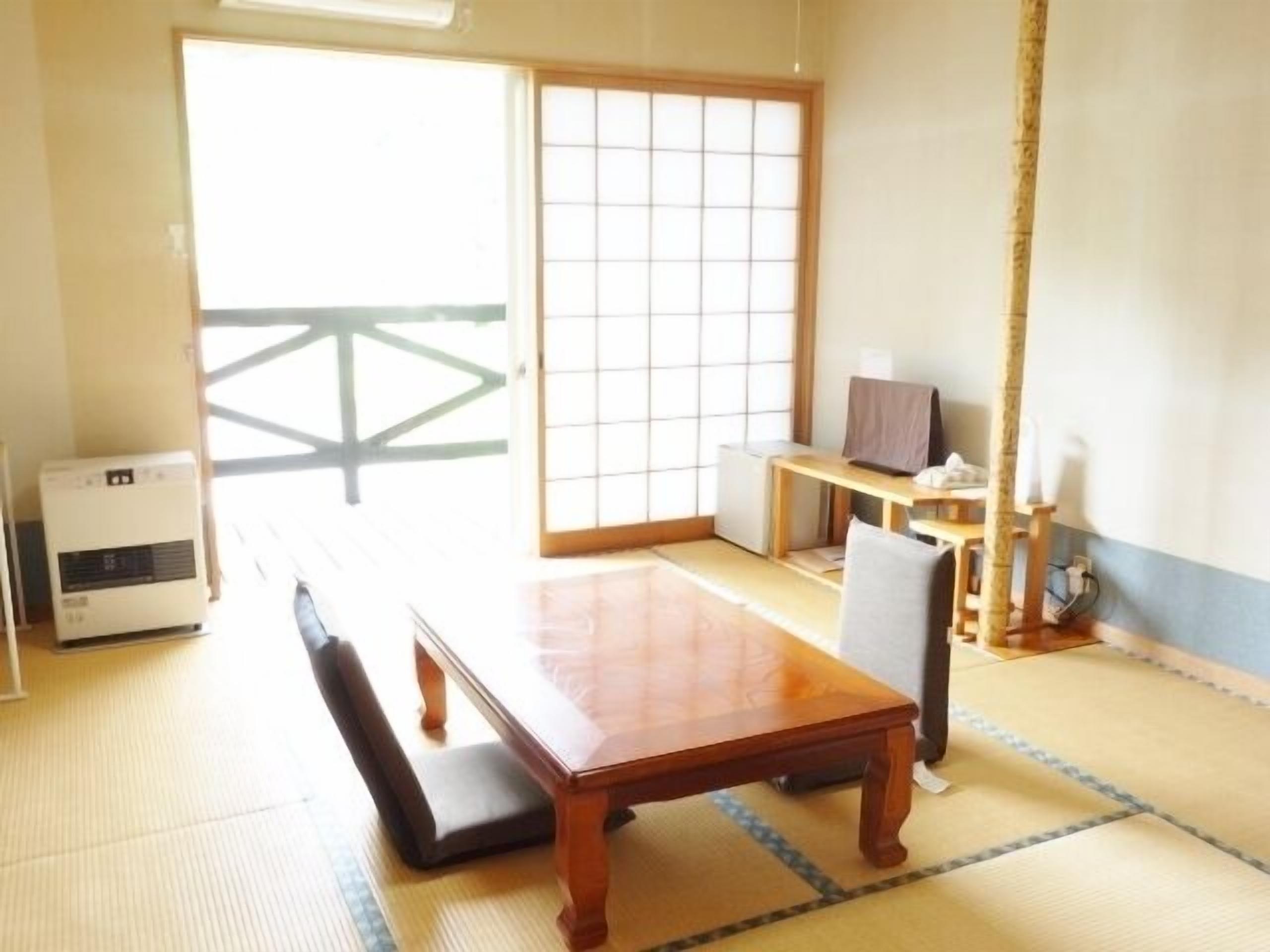 Um quarto japonês tradicional, com tatames, uma mesa baixa, um banco, uma televisão e uma porta deslizante.