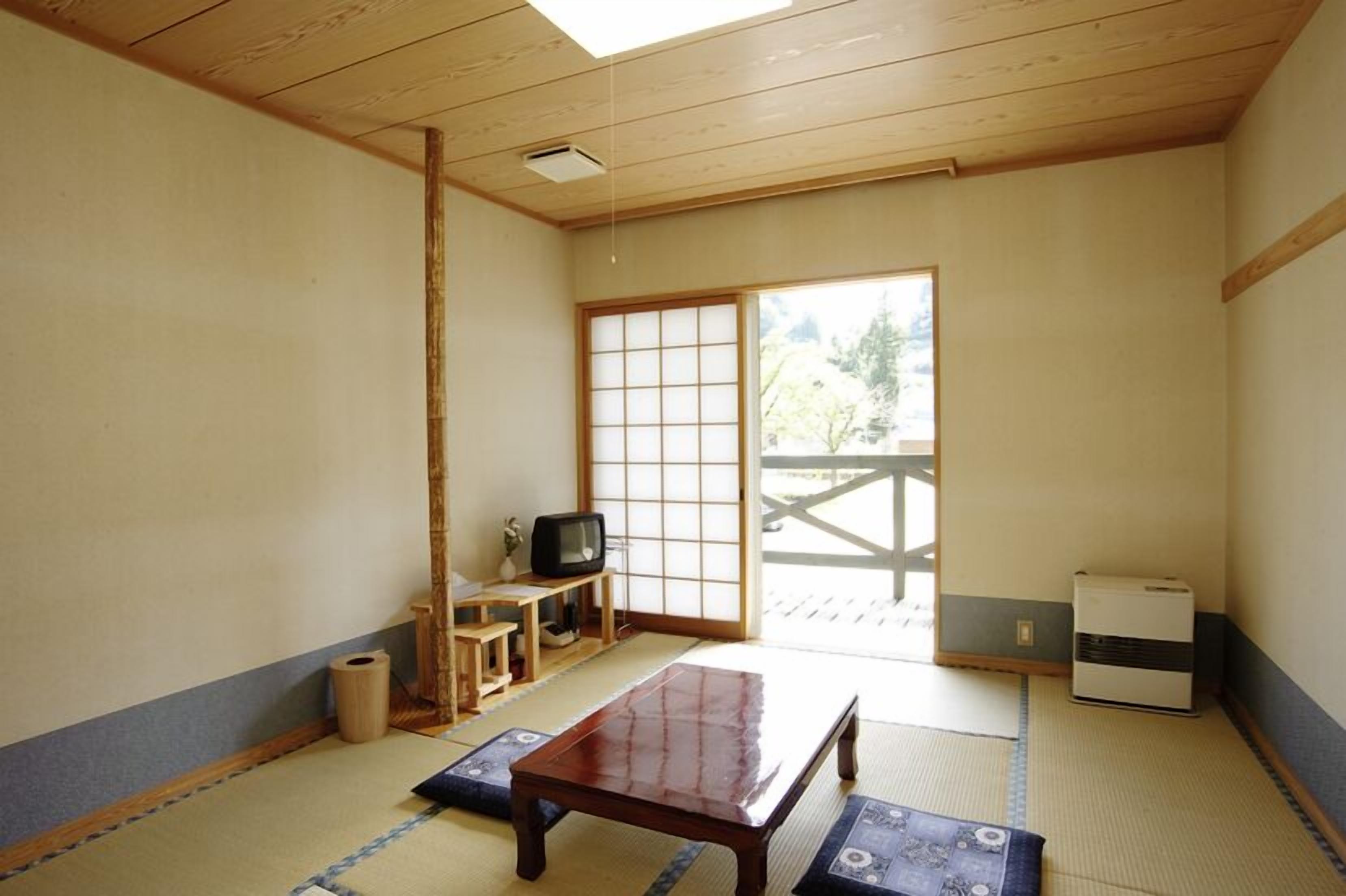 Quarto japonês tradicional com tatames, uma mesa de tatame, televisão, aquecedor e porta deslizante para uma varanda.