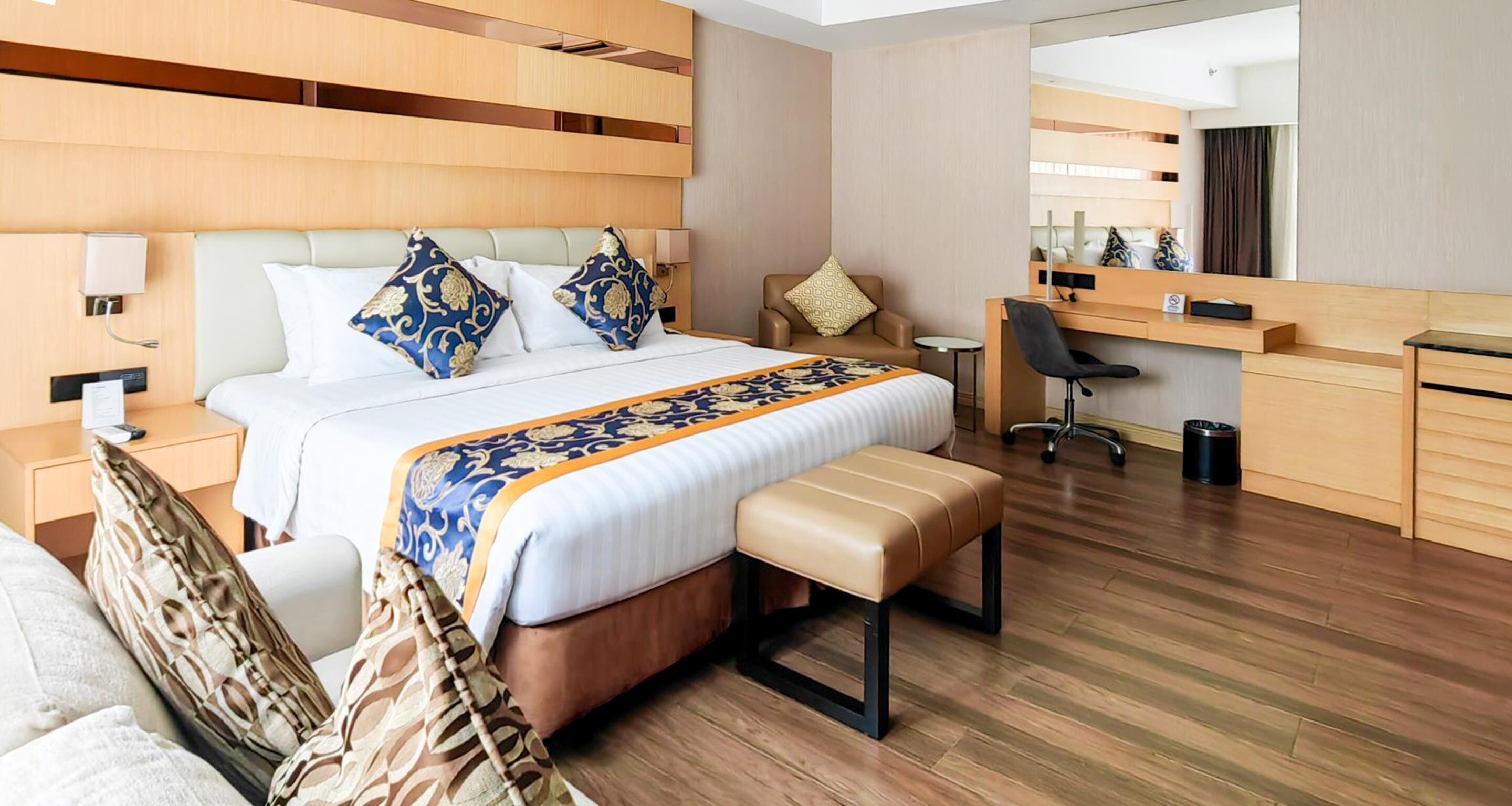 Quarto de hotel com cama, mesa de cabeceira, cadeira, escrivaninha e espelho.