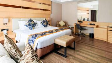 Quarto de hotel com cama, mesa de cabeceira, cadeira, escrivaninha e espelho.