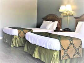 Quarto de hotel com duas camas, cada uma com saia verde e roupa de cama branca. Há uma mesa de cabeceira com abajur entre as camas.