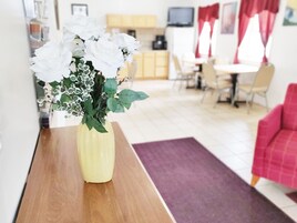 Quarto com mesa de madeira, um vaso amarelo com flores brancas, sofá vermelho e área de jantar com cadeiras e mesa.