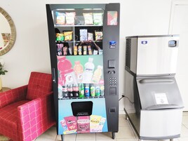 Máquina automática abastecida com lanches e bebidas, uma cadeira vermelha e um frigorífico.