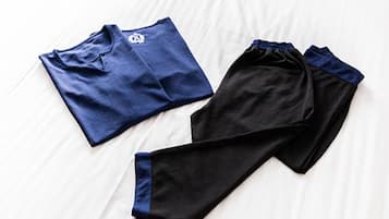 Cama com lençol branco e dois conjuntos de roupa de ginástica dispostos sobre ela.
