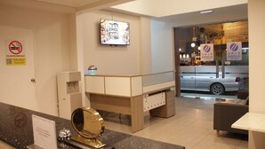 Uma área de recepção de hotel com balcão, televisão na parede e um carro visível pela janela.