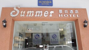 Exterior do Hotel Summer, com uma placa visível e duas lanternas de cada lado.