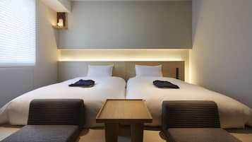 Quarto de hotel com duas camas, uma mesa pequena e duas cadeiras.