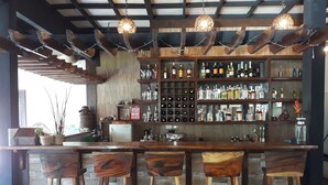 Uma área de bar com cadeiras de madeira, um balcão longo e prateleiras cheias de garrafas.