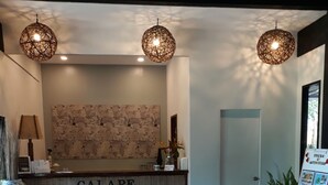 Uma receção com uma placa a indicar "Calape Forest Resort", duas luminárias esféricas penduradas, um mural com um mapa e uma planta em vaso à direita.
