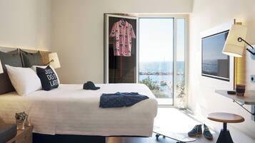 Quarto de hotel com uma cama, uma escrivaninha, uma cadeira, uma janela com vista e uma porta.