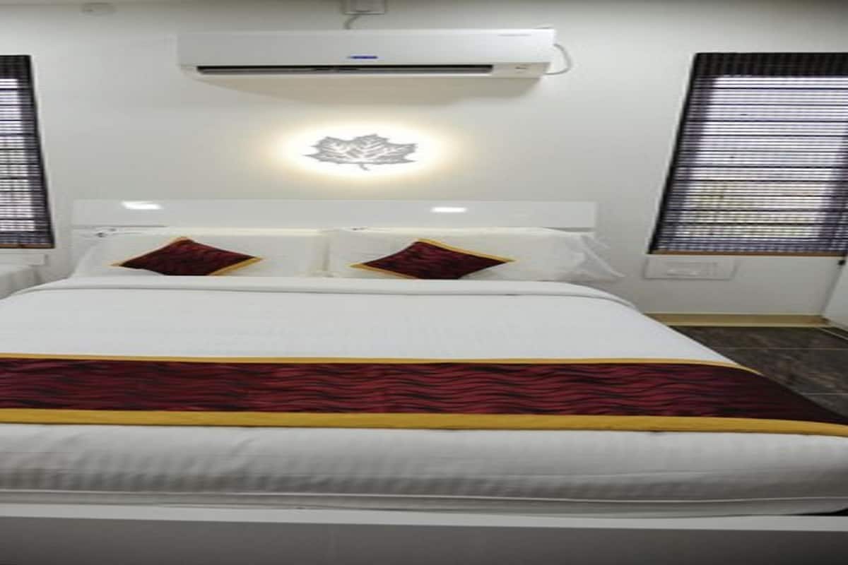 Quarto de hotel com uma cama, duas mesas de cabeceira, um ar condicionado e uma luminária fixada na parede.