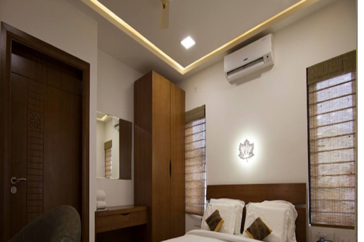 Quarto de hotel com cama, escrivaninha, cadeira, ar condicionado e janela com persianas.