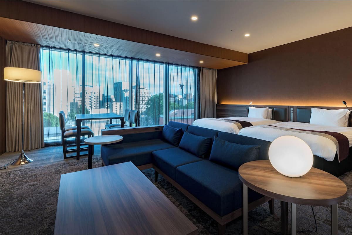 Quarto de hotel moderno com uma cama grande, um sofá, uma mesa de jantar e vista para a cidade.