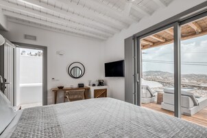 Quarto moderno com uma cama grande, uma escrivaninha, uma televisão e uma varanda com vista para a cidade.