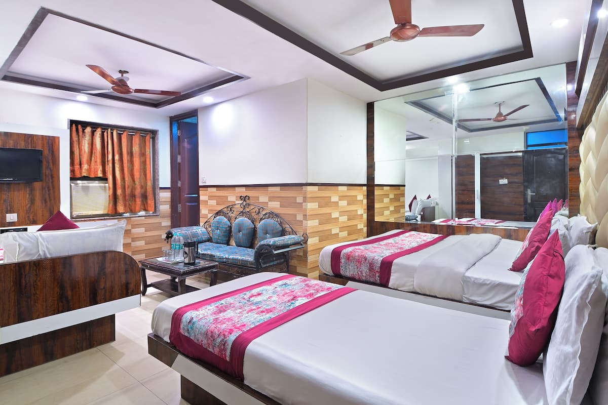 Quarto de hotel com duas camas, um sofá, uma televisão e um ventilador de teto.