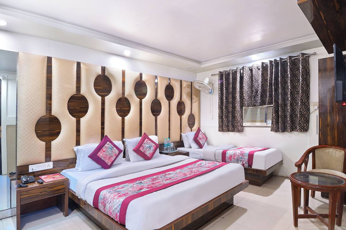 Quarto de hotel com duas camas, cabeceira de madeira, uma mesinha e uma cadeira.