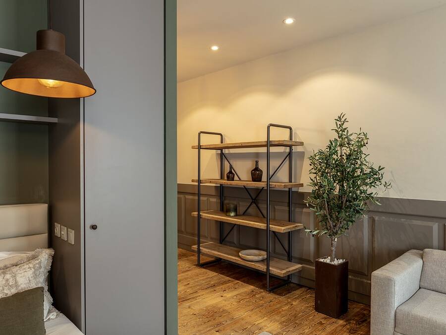 Quarto moderno com piso de madeira, estante de metal, planta em vaso e luminária pendente.