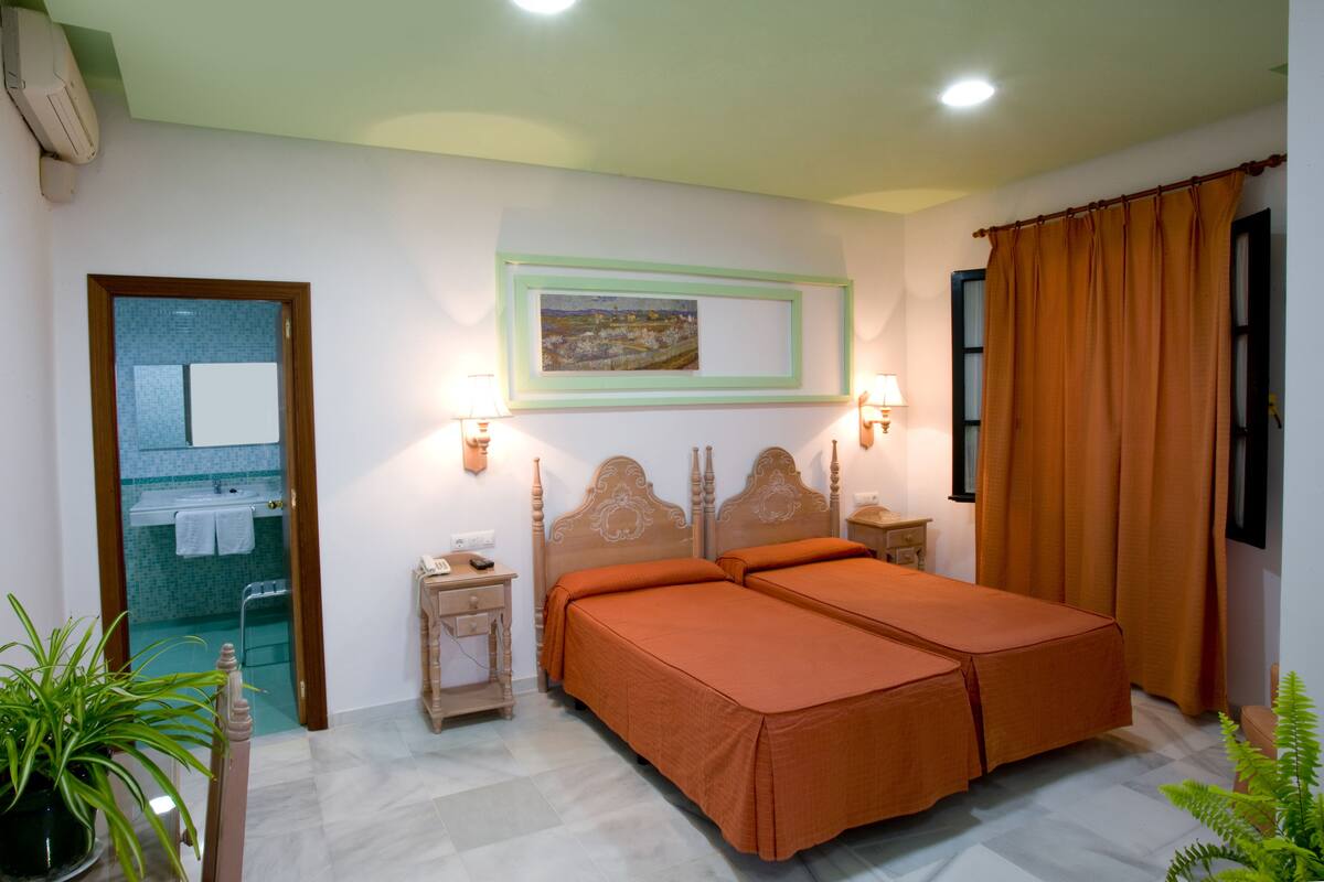 Quarto de hotel com duas camas, banheiro visível por uma porta aberta e um quadro na parede.