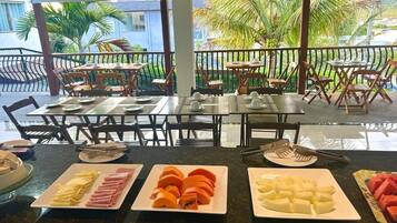 Disposição de buffet com diversos tipos de comida, mesas e cadeiras.