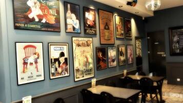 Interior de restaurante com uma parede decorada com cartazes antigos e uma área de estar com mesas e cadeiras.