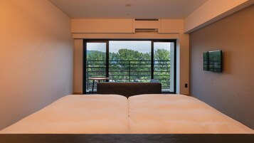 Quarto com cama, uma mesinha e vista para árvores através de uma janela grande.