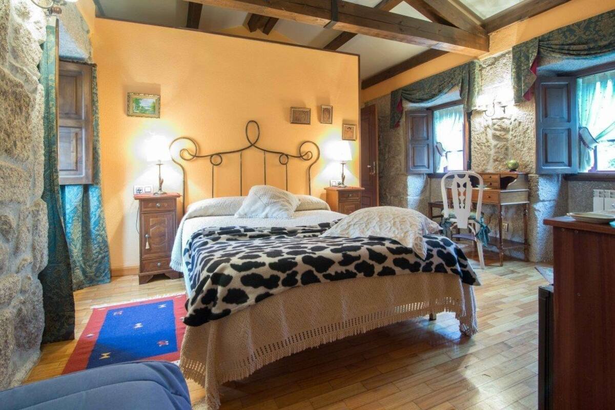 Um quarto aconchegante com cama, piso de madeira, paredes de pedra e uma janela com cortinas.