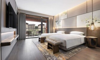 Quarto de hotel moderno com varanda, duas camas, televisão e vista para a paisagem urbana.