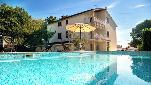 Piscina com piso revestido, edifício com varanda e mobiliário de exterior.
