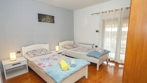 Quarto com duas camas, mesa de cabeceira, abajur, um quadro na parede e janela com cortinas.
