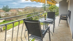 Varanda com duas cadeiras e uma mesa, com vista para uma paisagem cênica com casas e árvores.