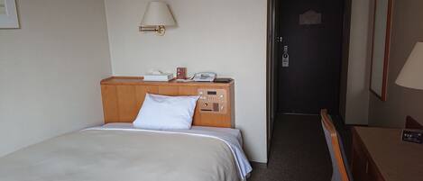 Quarto de hotel com cama, mesa de cabeceira, abajur e porta que dá para outro cômodo.