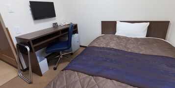 Quarto de hotel com cama, escrivaninha, cadeira, televisão e tomada.