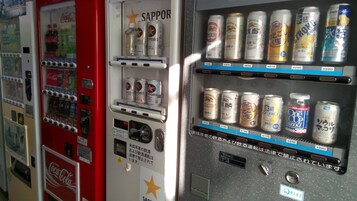 Máquinas automáticas com diversas bebidas e petiscos, incluindo Coca-Cola e cerveja Sapporo.