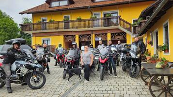 Um grupo de pessoas com motocicletas em frente a um prédio amarelo com varanda.
