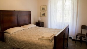 Quarto com cama de madeira, mesa de cabeceira, cadeira e duas molduras na parede.