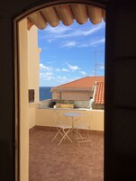 Uma varanda com chão de azulejos, uma mesa com duas cadeiras e vista para o mar.