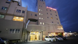 Um hotel com vários andares, uma entrada destacada e diversos carros estacionados em frente.